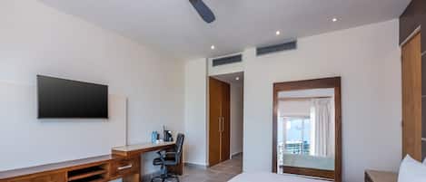 Quarto de hotel moderno com cama, escrivaninha, cadeira, televisão, guarda-roupa e ventoinha no teto.