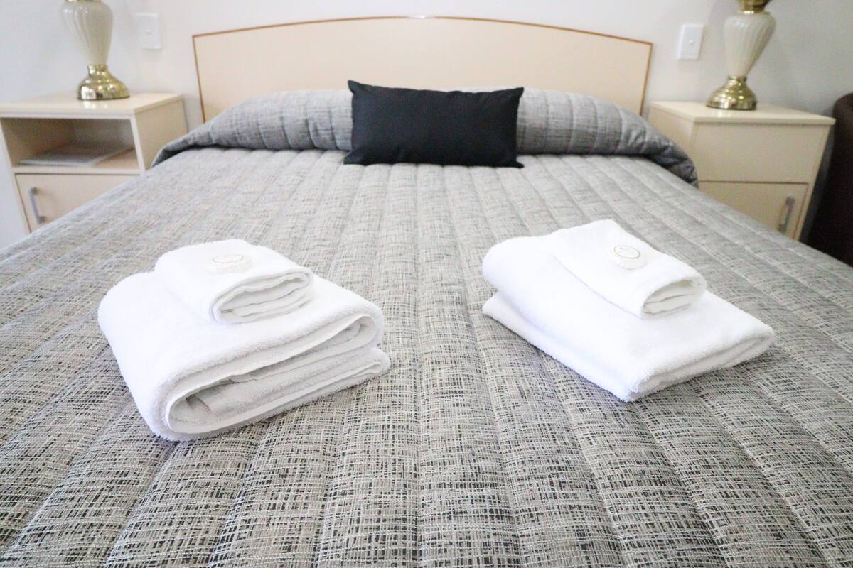 Cama bem arrumada com duas toalhas dobradas e um travesseiro preto.