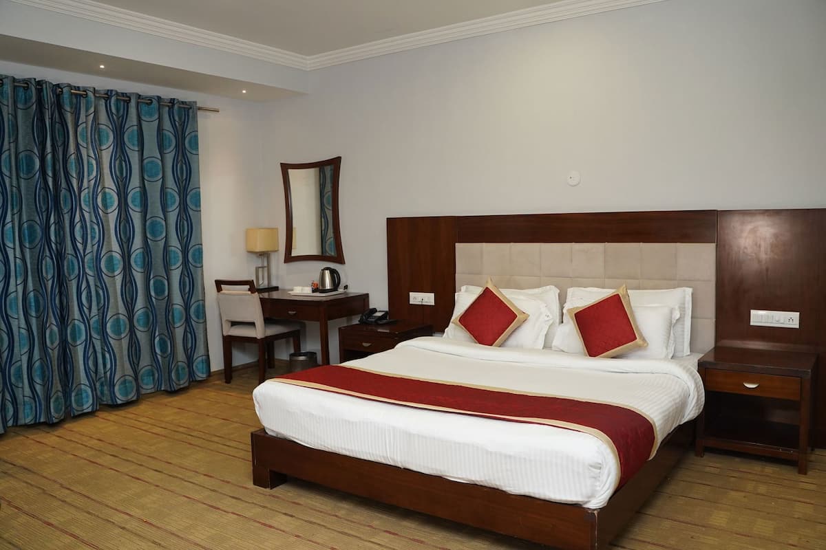 Quarto de hotel com uma cama grande, uma escrivaninha, uma cadeira, um espelho e uma mesa de cabeceira.