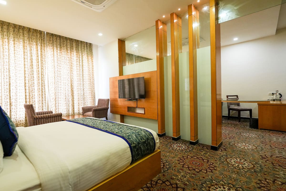Quarto de hotel com cama, televisão presa na parede, escrivaninha e cadeira.