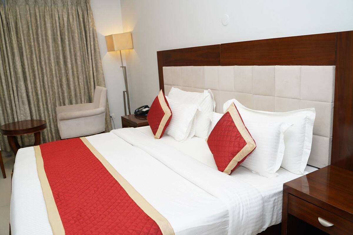 Quarto de hotel com cama, uma cadeira, uma luminária e uma mesa de cabeceira.
