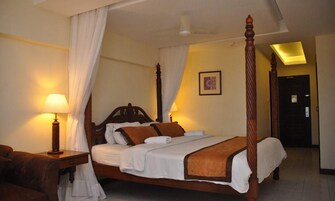 Uma cama com dossel, roupa de cama branca, cabeceira de madeira e uma mesinha de cabeceira com abajur.