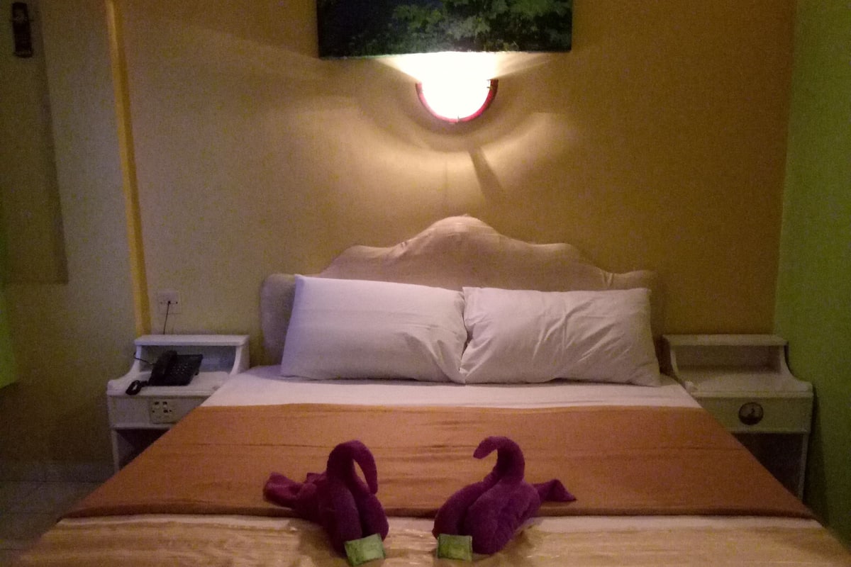 Quarto de hotel com uma cama, duas mesas de cabeceira, uma luminária na parede e um quadro sobre a cama.