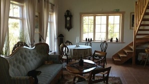 Um quarto aconchegante com sofá, mesa redonda com cadeiras, relógio na parede e escada.