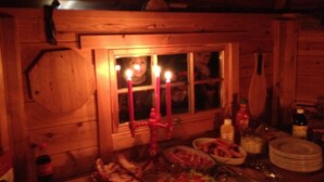 Interior de uma cabana de madeira com janela, velas e uma mesa com comida e bebidas.