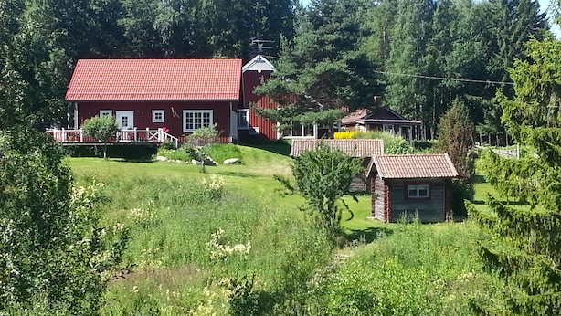 Uma casa vermelha com telhado de telhas, rodeada por vegetação e árvores.