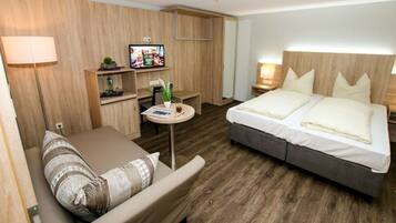 Quarto de hotel compacto com cama, sofá, pequena mesa, televisão e guarda-roupa.