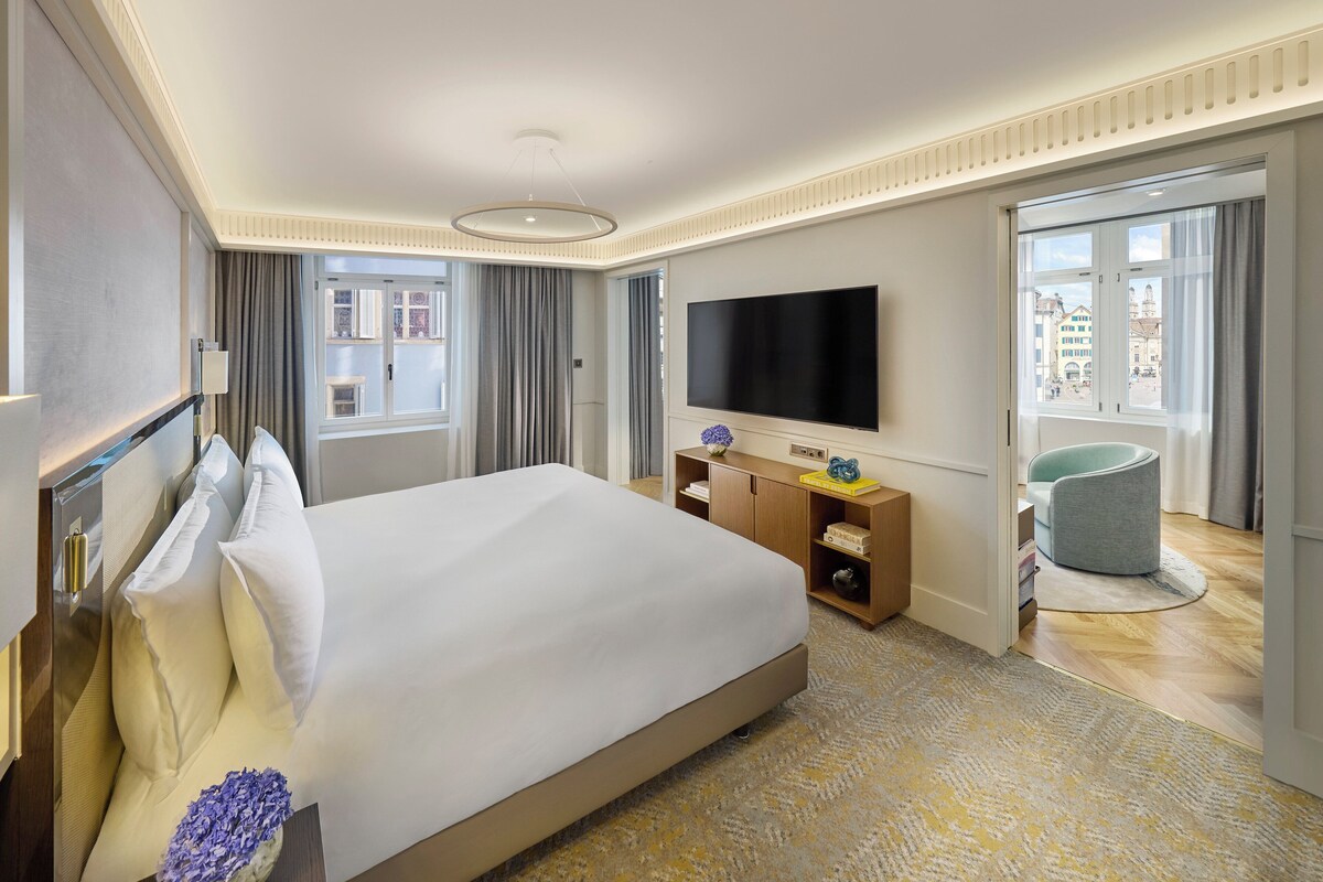 Quarto de hotel com uma cama grande, televisão de tela plana, escrivaninha com computador e vista da cidade pela janela.