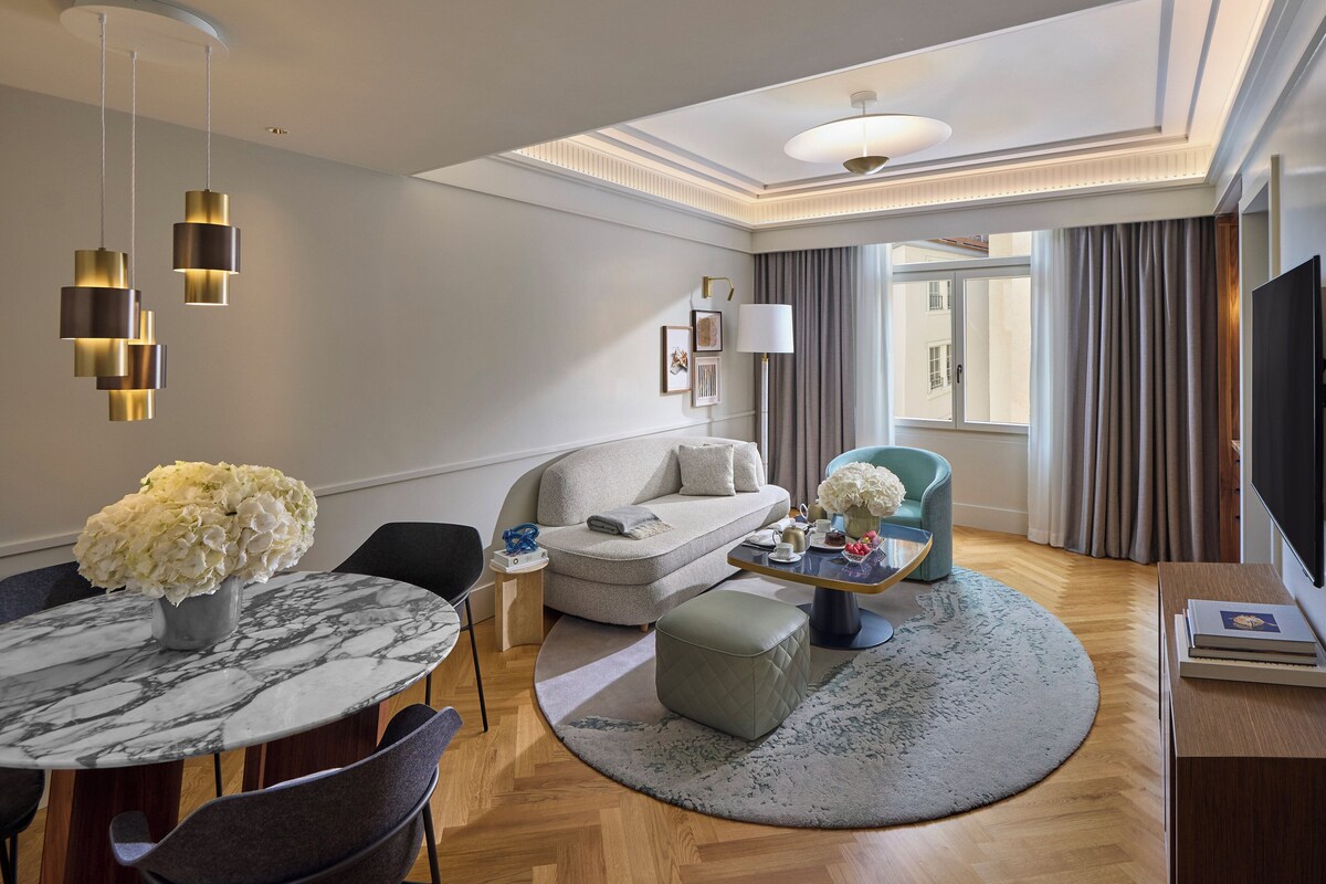 Uma sala de estar moderna com uma mesa de mármore, um sofá cinzento, uma poltrona verde-água e uma TV de tela plana.