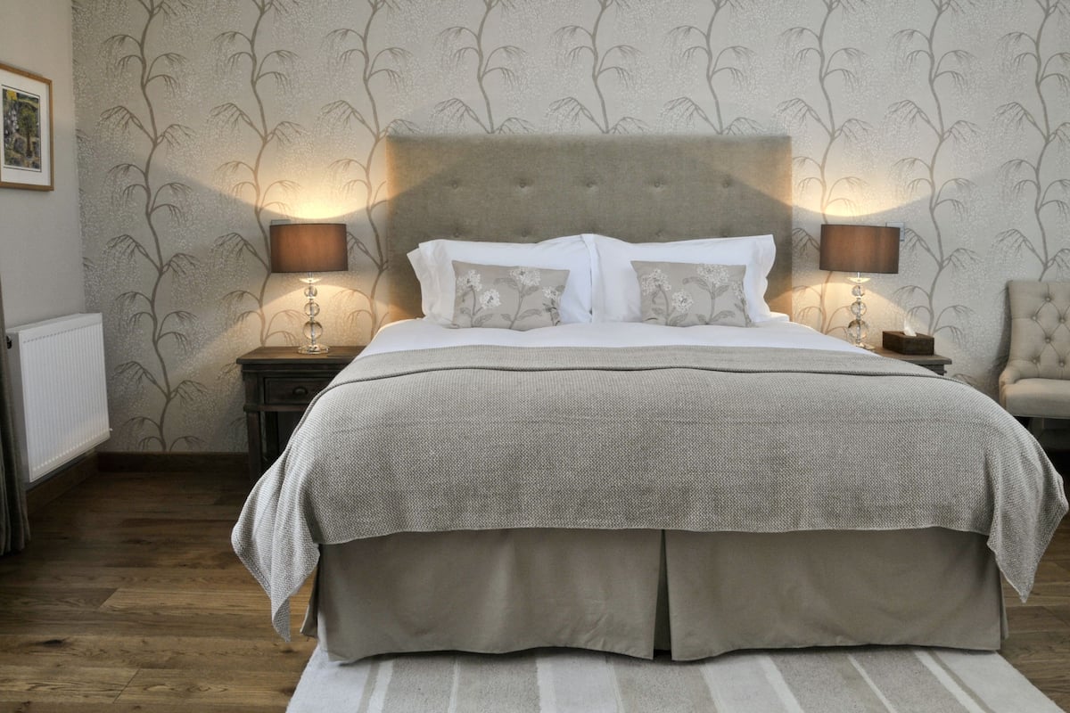 Um quarto bem arrumado com uma cama grande, duas mesas de cabeceira com abajures, uma cadeira e um radiador.