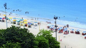 Uma praia com guarda-sóis e cadeiras, e pessoas nadando na água.