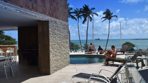 Área de piscina externa com espreguiçadeiras, churrasqueira e vista para o mar.