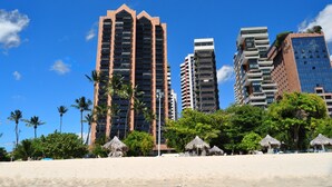 Um hotel à beira-mar com vários edifícios altos, palmeiras e guarda-sóis de palha.