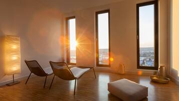 Quarto moderno com duas janelas amplas, luminária de pé e um banco estofado.