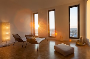 Quarto moderno com duas janelas amplas, luminária de pé e um banco estofado.