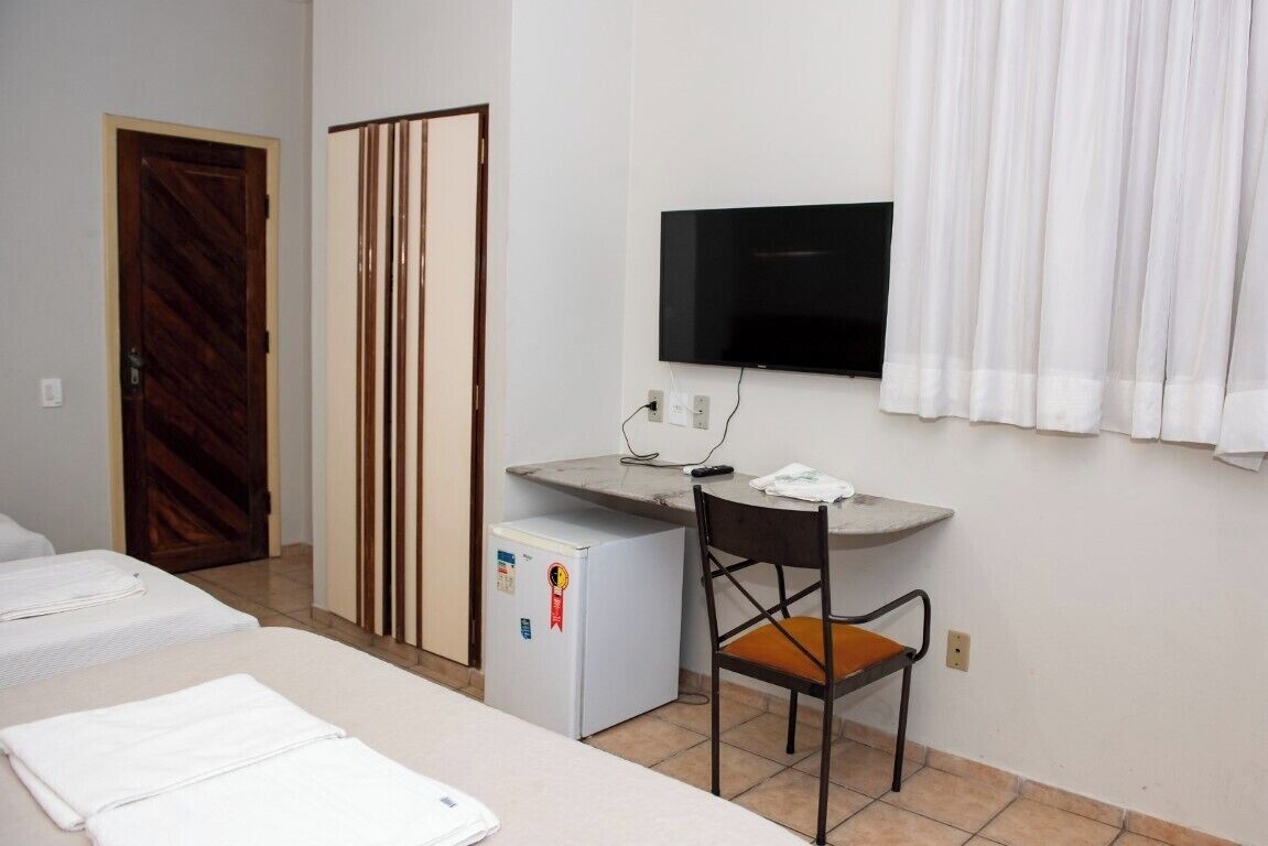 Quarto de hotel com cama, escrivaninha com cadeira, televisão e minibar.