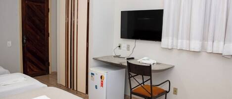 Quarto de hotel com cama, escrivaninha com cadeira, televisão e minibar.