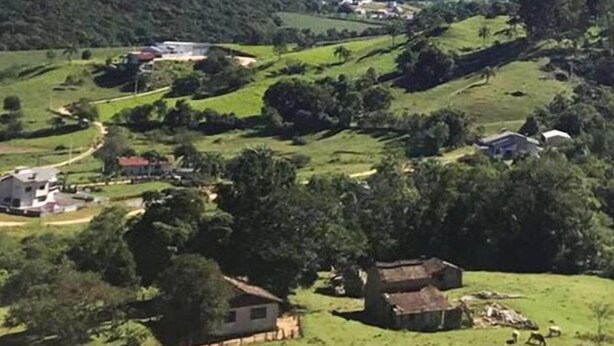 Paisagem rural com colinas onduladas, casas espalhadas e céu claro.