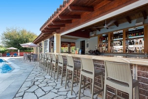 Uma área de bar com disposição de assentos à beira da piscina e um balcão.