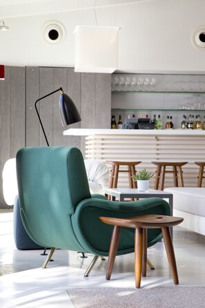 Uma sala de estar moderna com uma poltrona verde-água, uma pequena mesa lateral de madeira e um abajur preto.