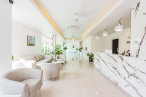 Um hall de hotel moderno com uma recepção de mármore, várias áreas de estar e ventiladores de teto.
