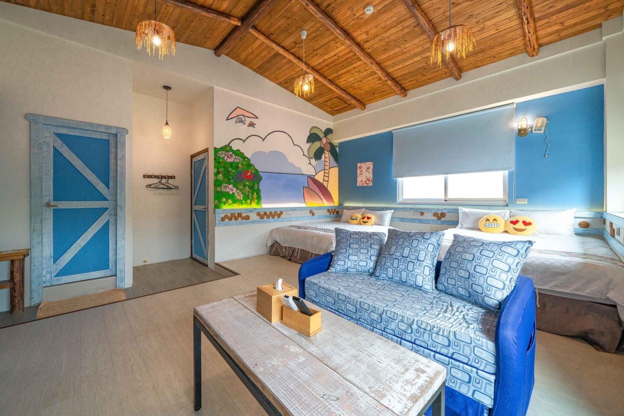 Um quarto aconchegante com teto de madeira, porta com moldura azul, cama com roupa de cama estampada, sofá azul e uma pequena mesa com caixa de lenços.