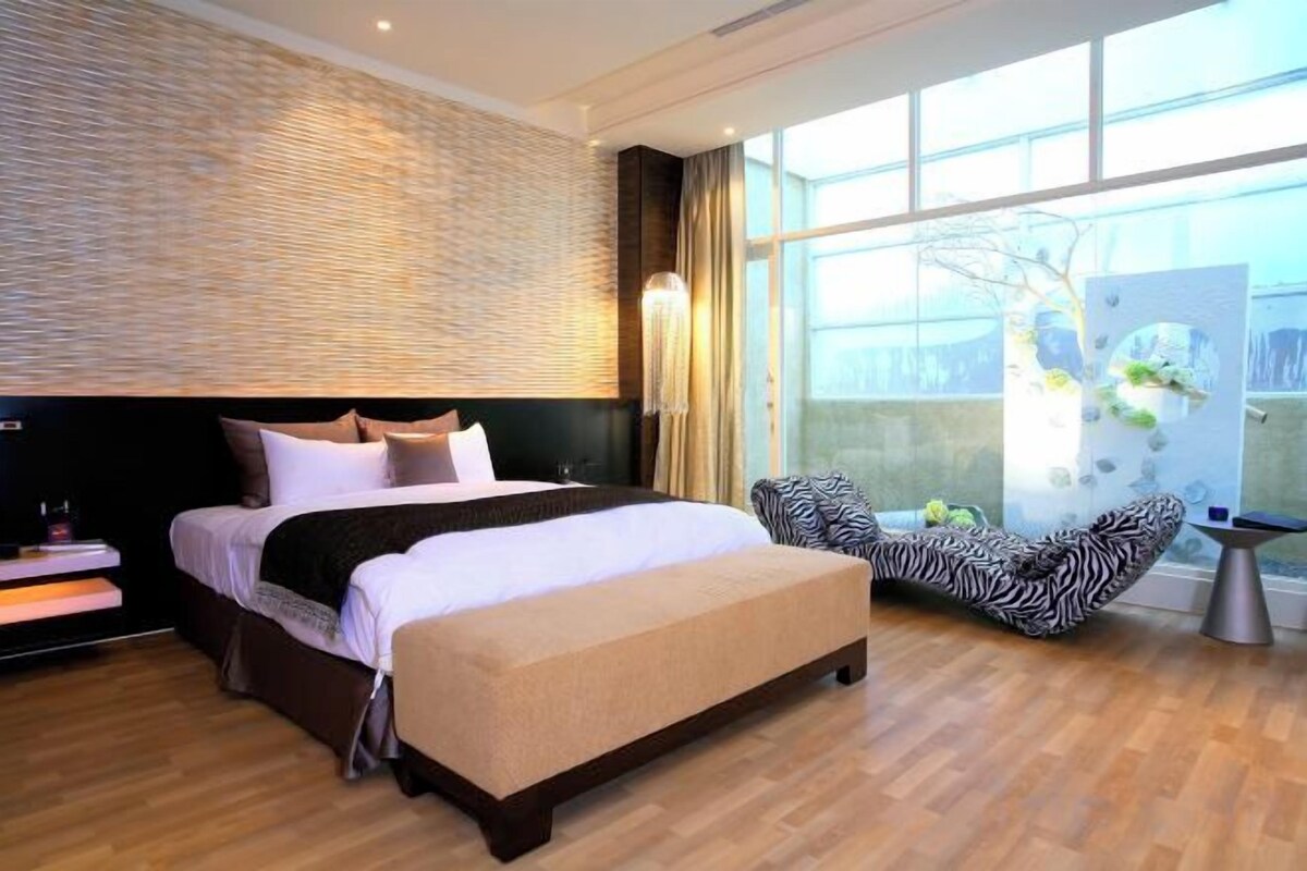 Quarto de hotel moderno com uma cama grande, um espaço de estar e vista pela janela.