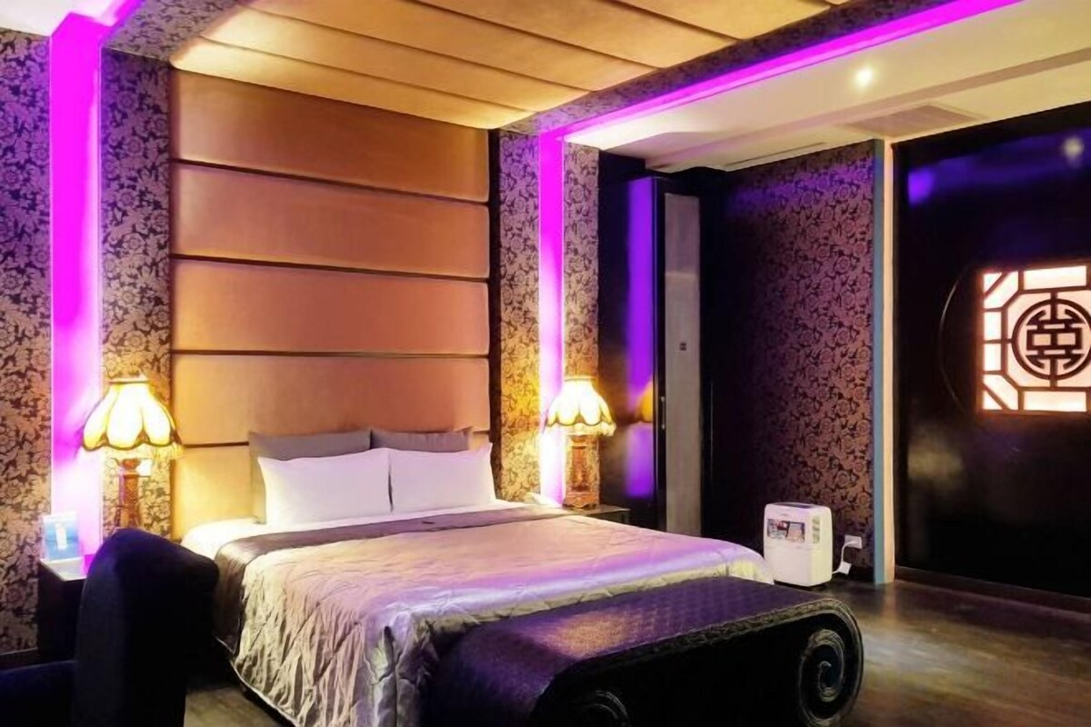 Quarto de hotel moderno com uma cama grande, duas luminárias de cabeceira, um criado-mudo e um painel decorativo na parede.