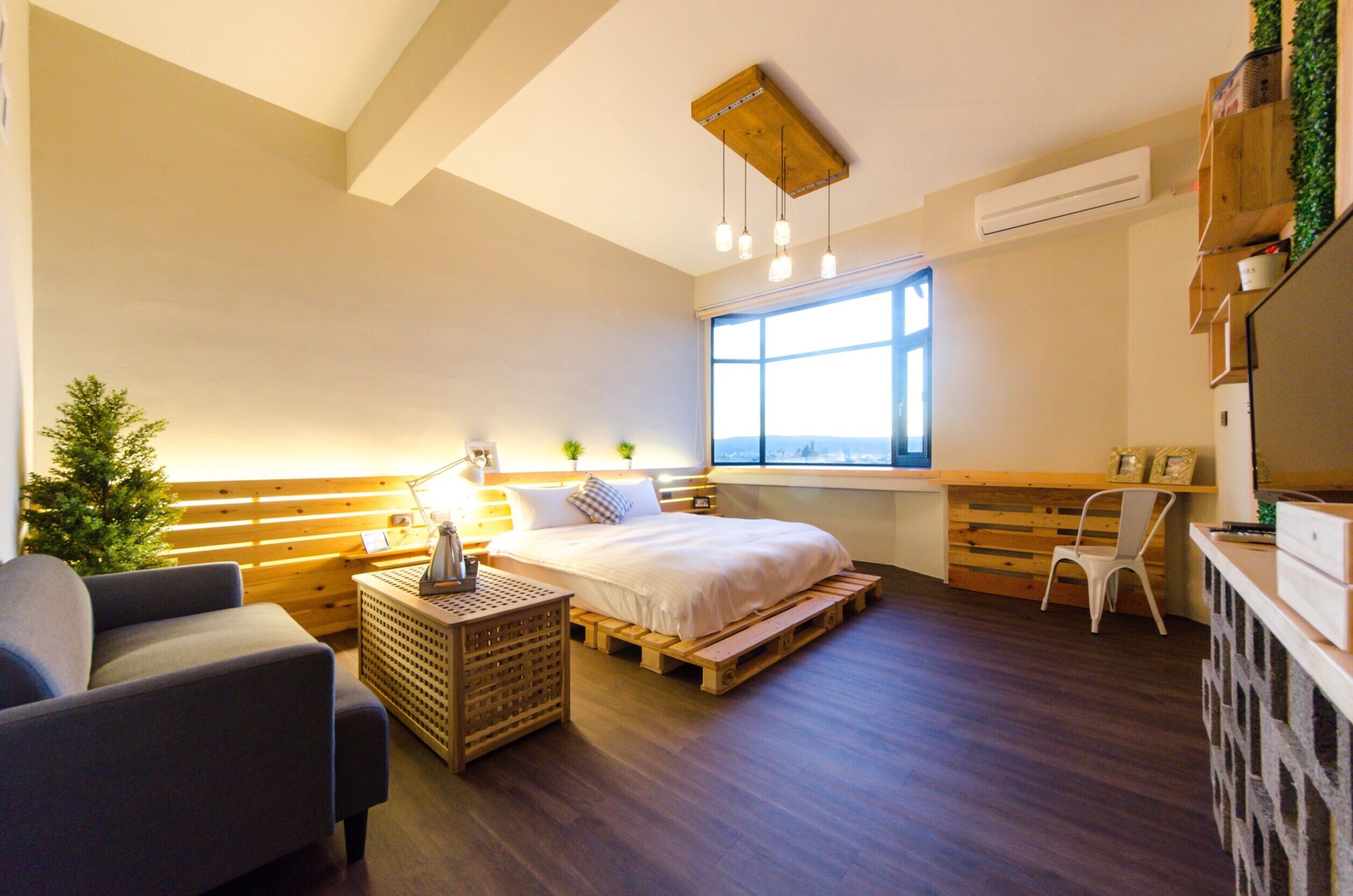 Quarto com cama, uma cadeira, mesa pequena, janela e cabeceira de madeira.
