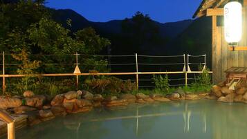 Um onsen japonês tradicional com um pavilhão de banho de madeira, um caminho de pedra e uma cerca de madeira.