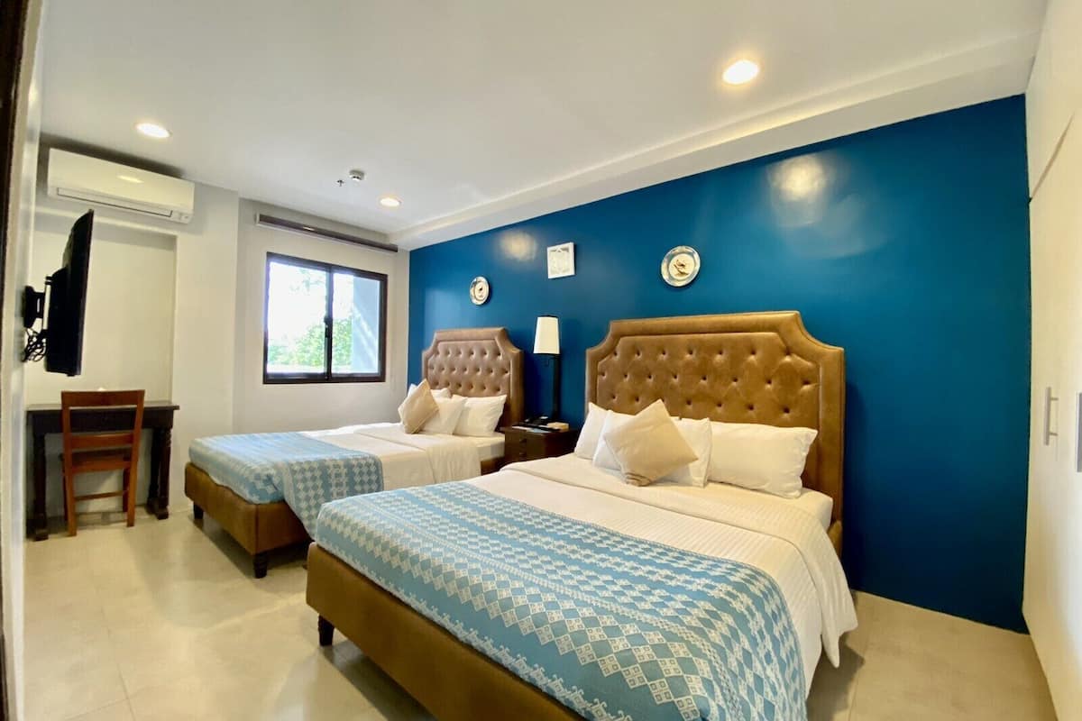 Quarto de hotel com duas camas, uma mesa e uma cadeira.