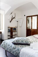 Quarto com cama, guarda-roupa de madeira, prateleira na parede e um objeto decorativo na parede.