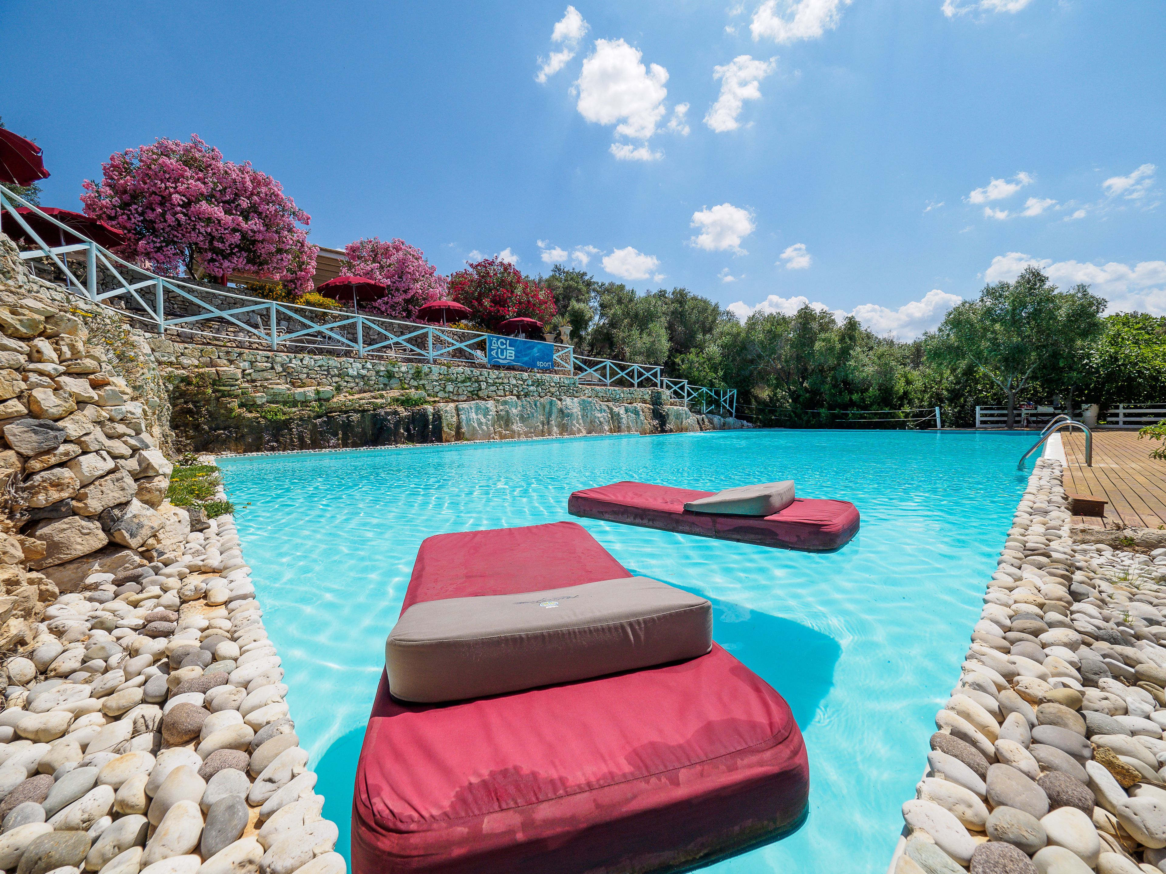 Piscina com cadeiras de sol vermelhas e uma parede de pedra.