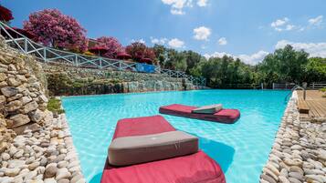 Piscina com cadeiras de sol vermelhas e uma parede de pedra.