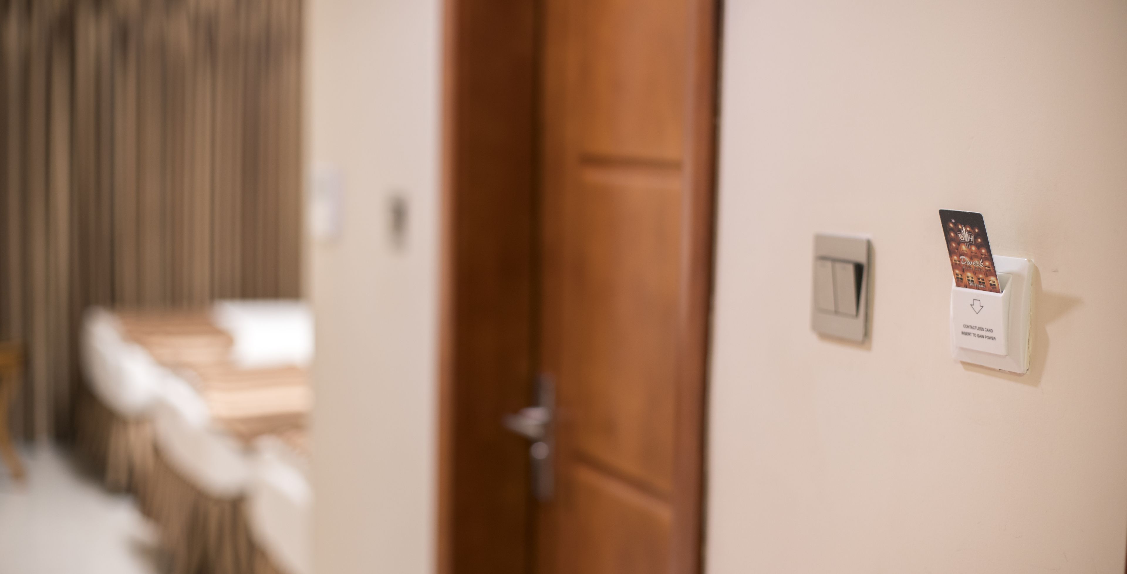 Corredor de hotel com porta de madeira, interruptor de luz e porta-cartões com um cartão.
