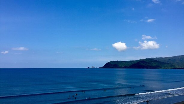 Uma praia com águas azul-claras e uma montanha ao longe.