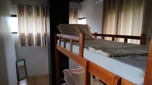 Quarto individual com beliche de madeira, um pequeno espelho e janela com cortinas.