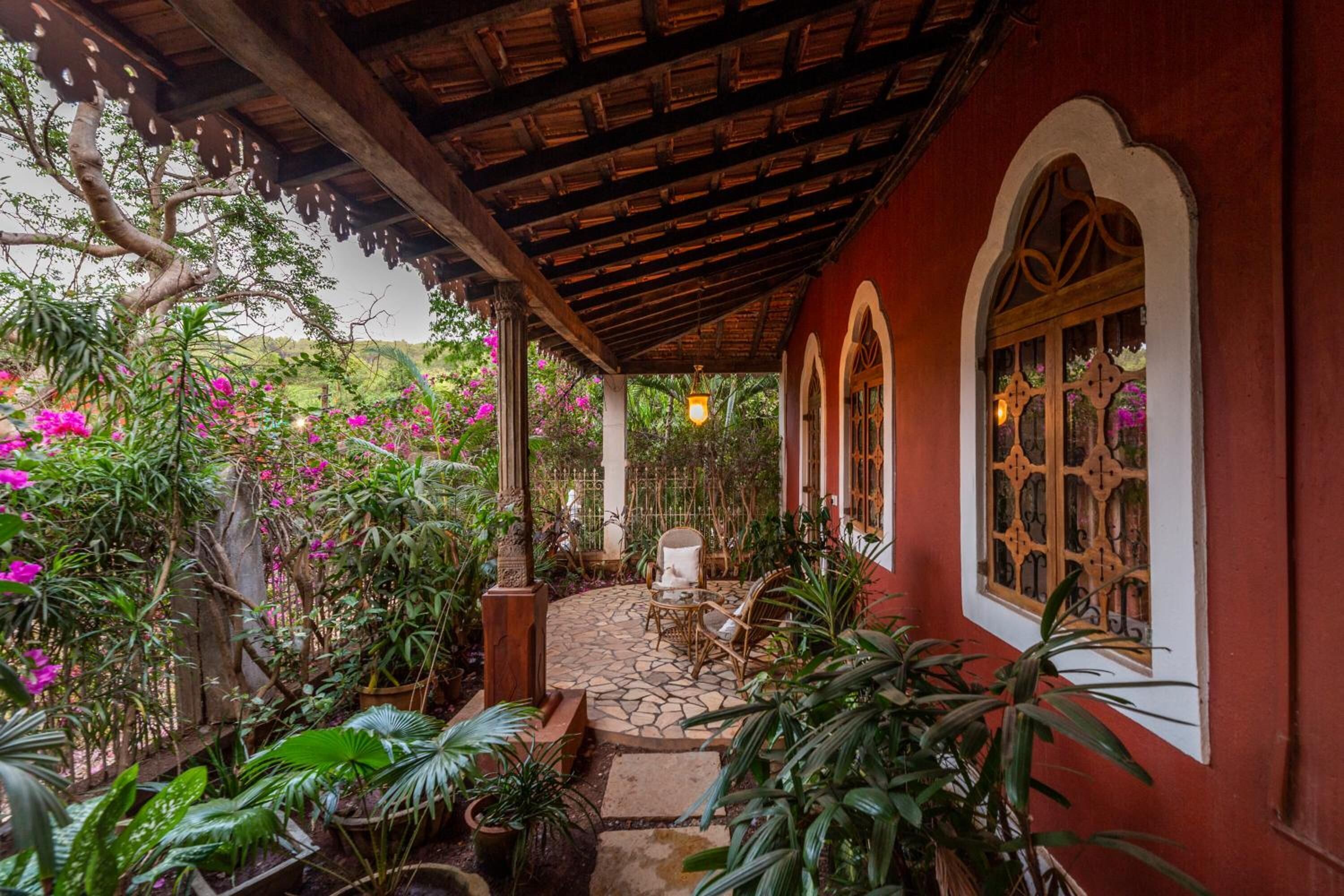 Uma área externa coberta com piso de pedra, rodeada por vegetação exuberante e plantas floridas.