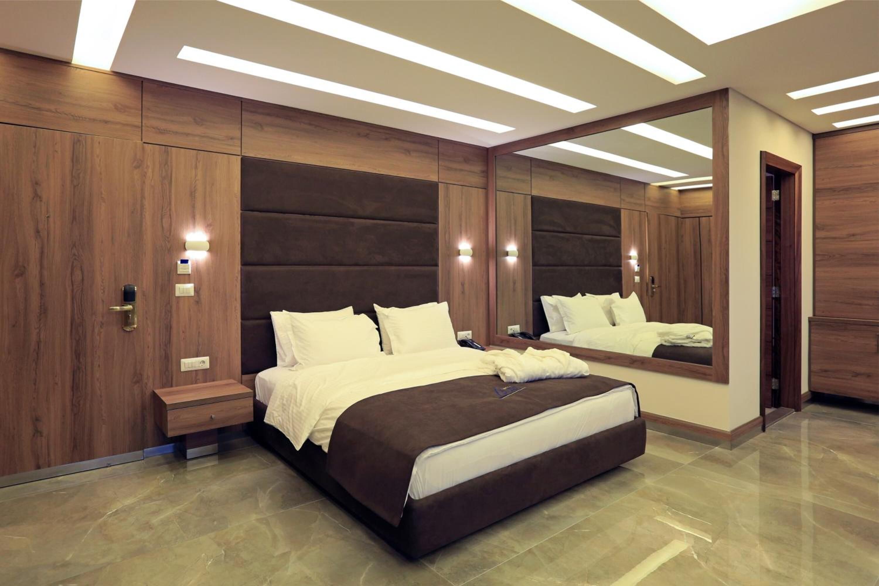 Quarto moderno com cama grande, painéis de madeira e iluminação embutida.