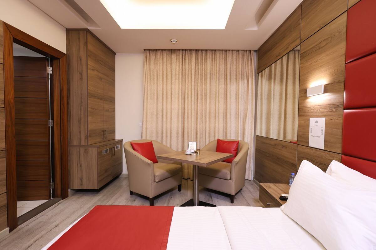 Quarto de hotel com cama, duas poltronas, uma mesinha, espelho e guarda-roupa.
