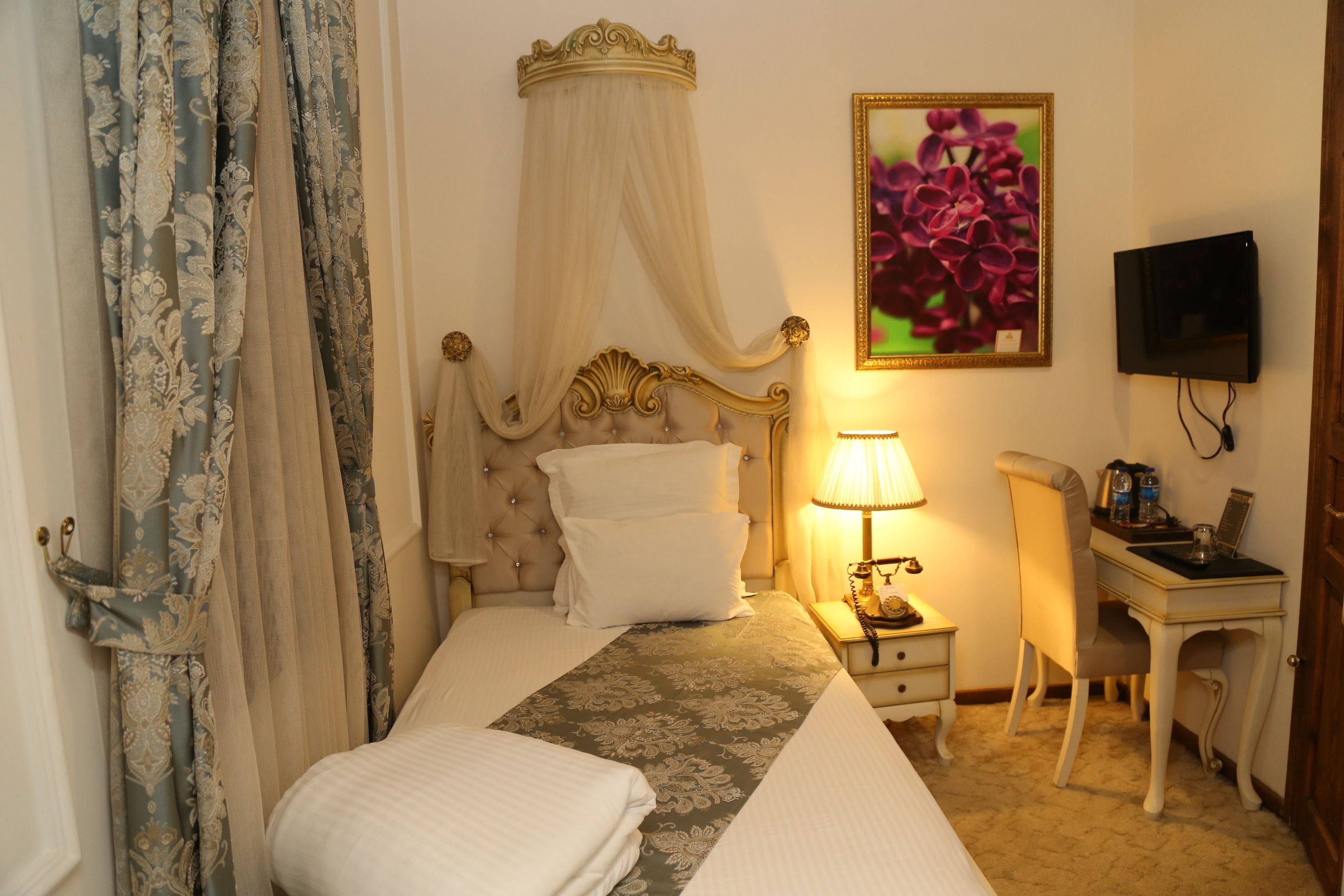 Quarto de hotel bem arrumado com uma cama de dossel, uma escrivaninha com cadeira, televisão e uma obra de arte floral emoldurada na parede.