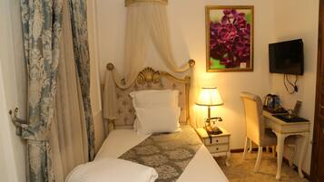 Quarto de hotel bem arrumado com uma cama de dossel, uma escrivaninha com cadeira, televisão e uma obra de arte floral emoldurada na parede.