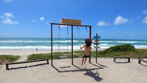 Cena de praia com baloiço e placa a indicar 'Barrada de São Miguel'.