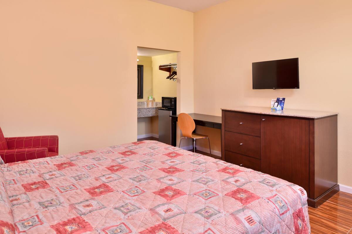Quarto de hotel com cama, escrivaninha, cadeira, televisão e cómoda.
