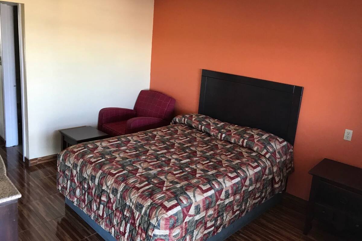Um quarto com cama, uma cadeira, uma mesinha e um armário.