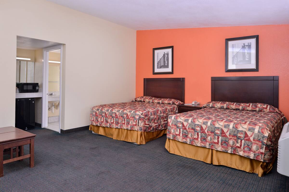 Quarto de hotel com duas camas, uma escrivaninha e um micro-ondas.