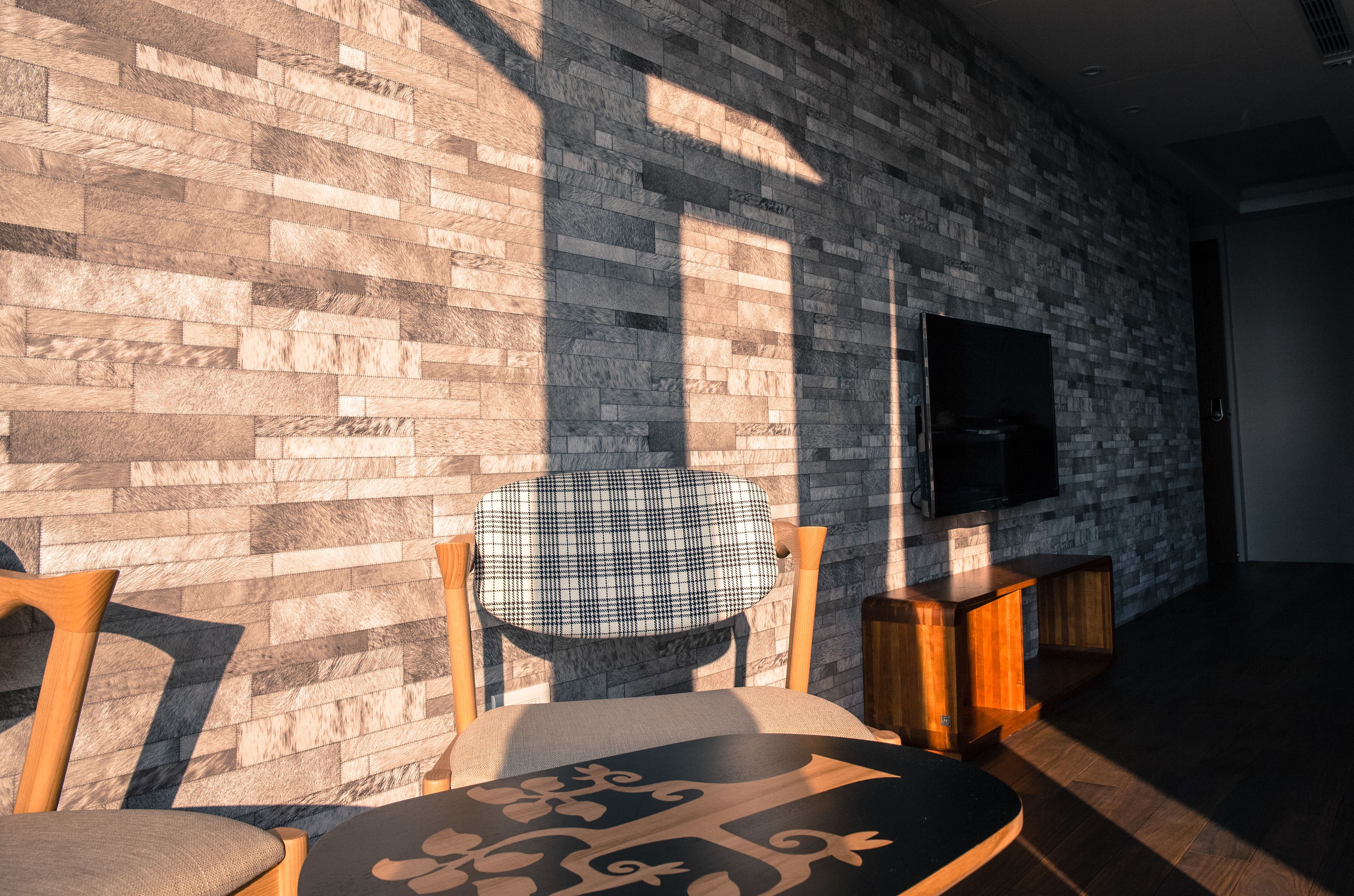 Uma sala de estar moderna com parede em padrão de tijolos, uma TV de tela plana na parede e uma mesa de centro de madeira com um jogo americano estampado.