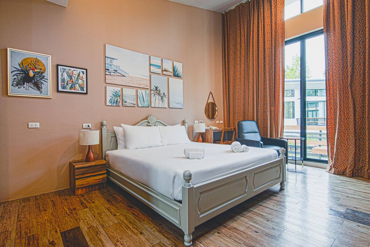 Quarto de hotel com uma cama grande, mesa de cabeceira com abajur, obra de arte na parede e vista para o exterior.