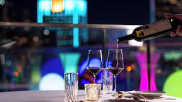Uma garrafa de vinho sendo servida em copos sobre uma mesa, com vista para a cidade ao fundo.