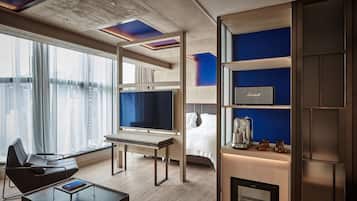 Quarto de hotel moderno com uma janela grande, televisão de tela plana, cama, máquina de café e minibar.